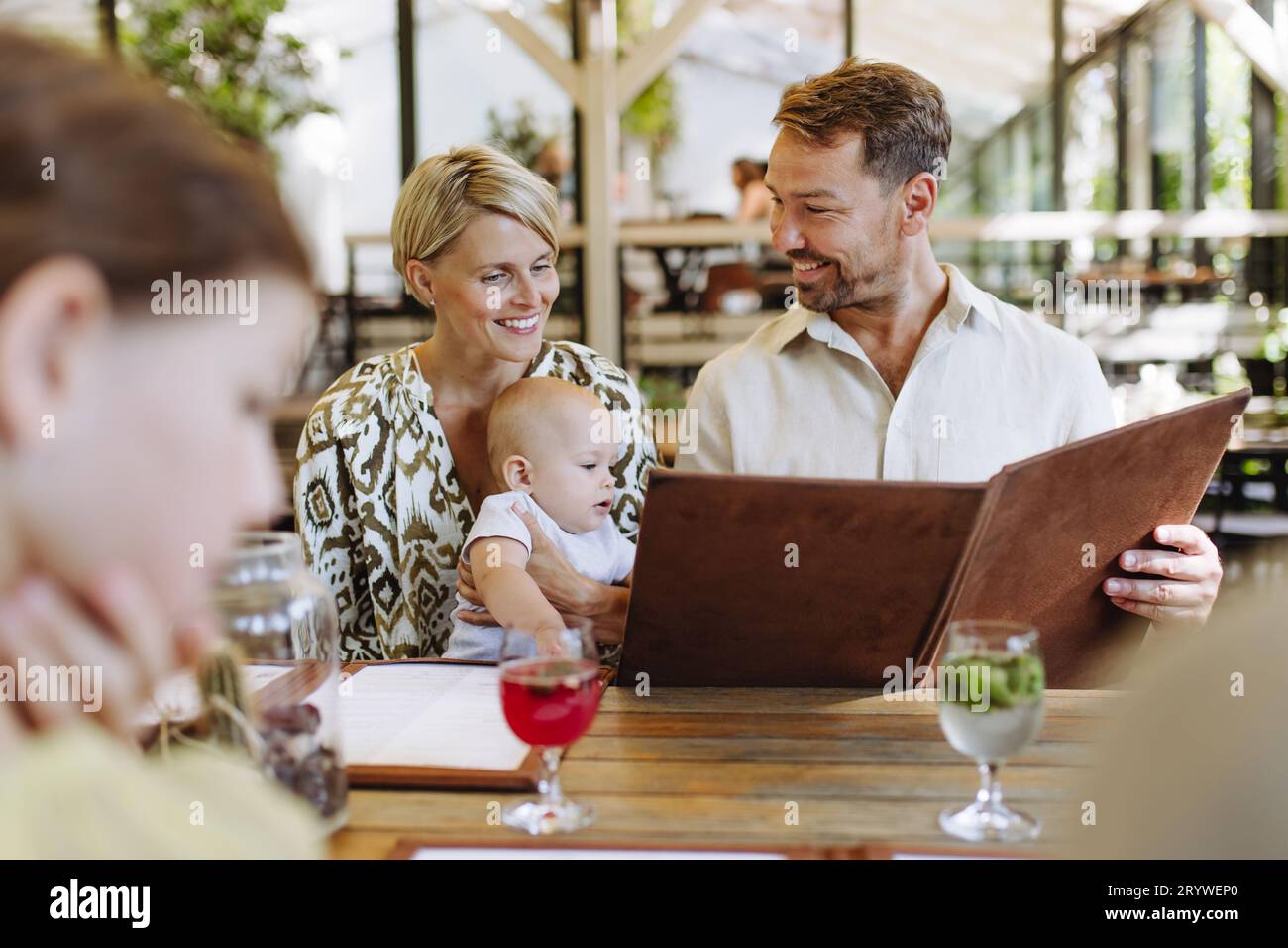 Family with baby reading menus in a restaurant, choosing food and ...