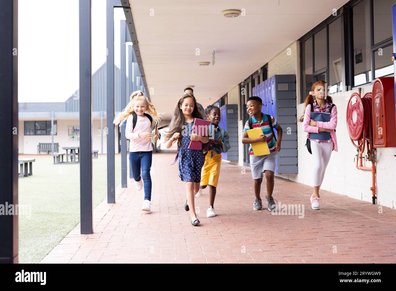 Diverse male teacher with happy children running in elementary school ...