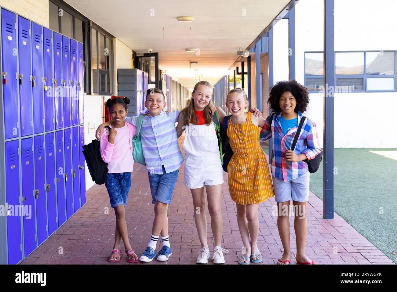 Portrait of five happy, diverse children with arms around shoulders in ...