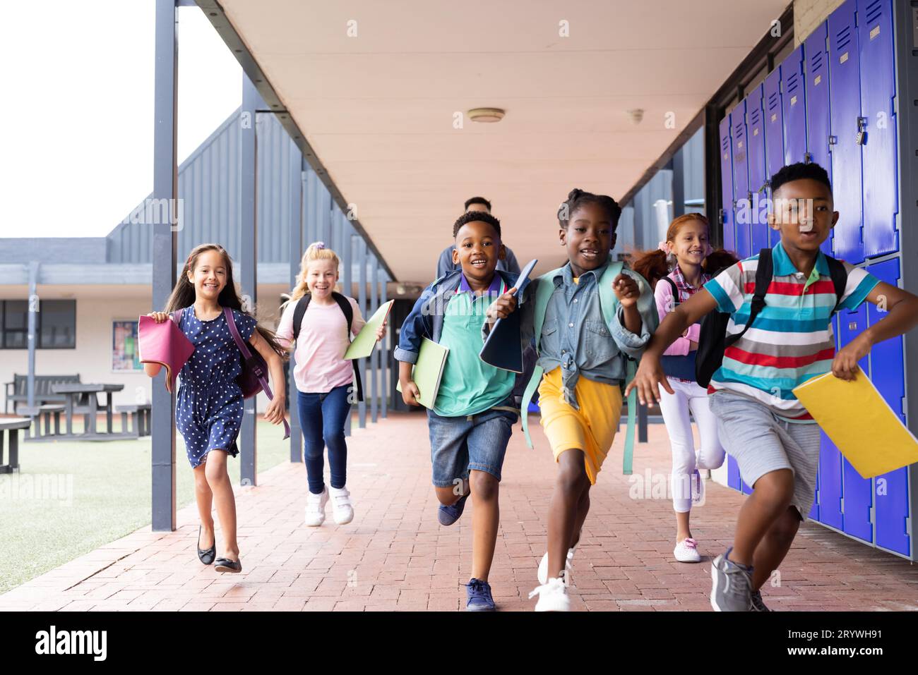 Diverse male teacher with happy children running in elementary school ...