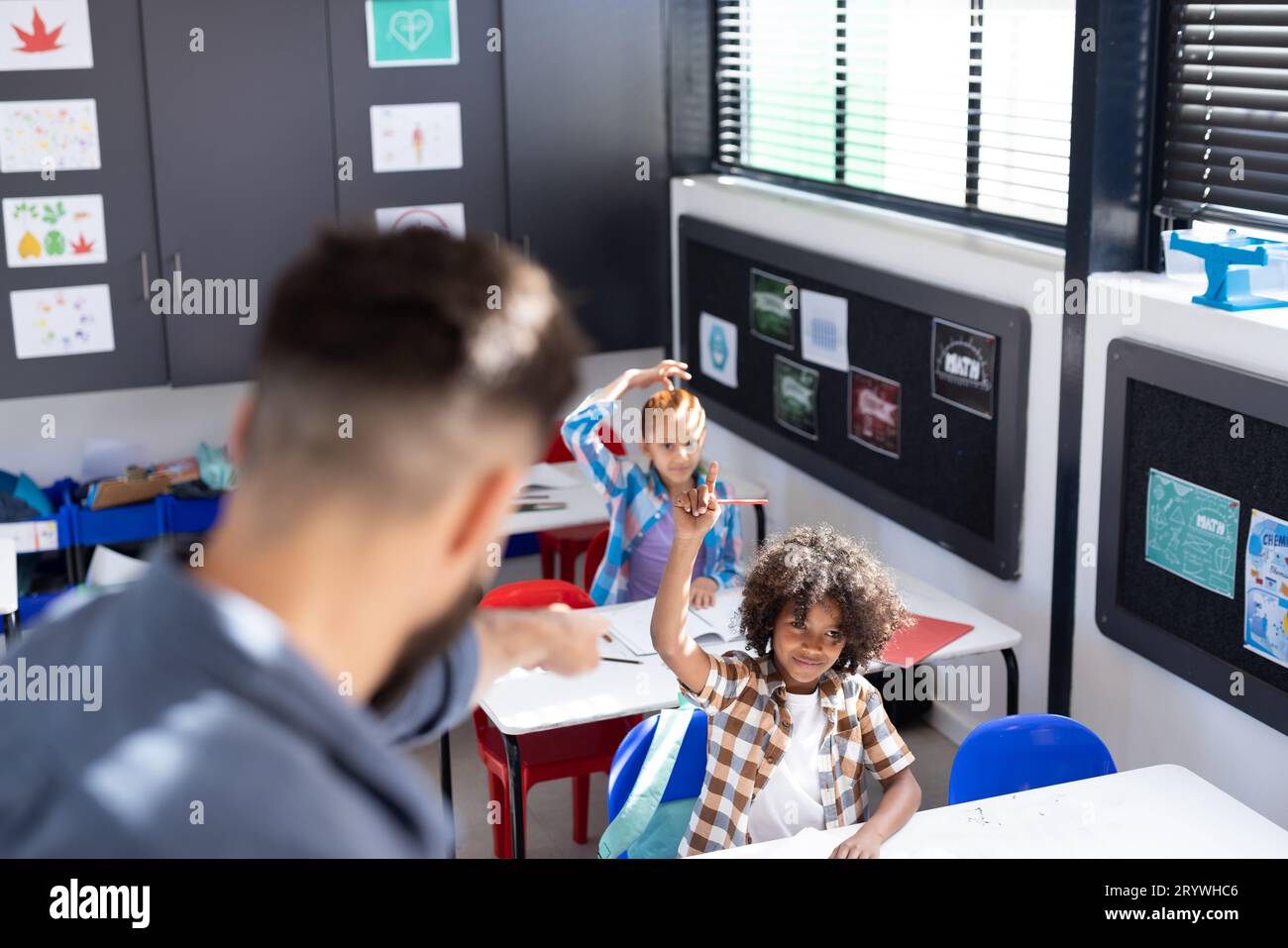 Diverse male teacher and schoolchildren raising hands in elementary ...
