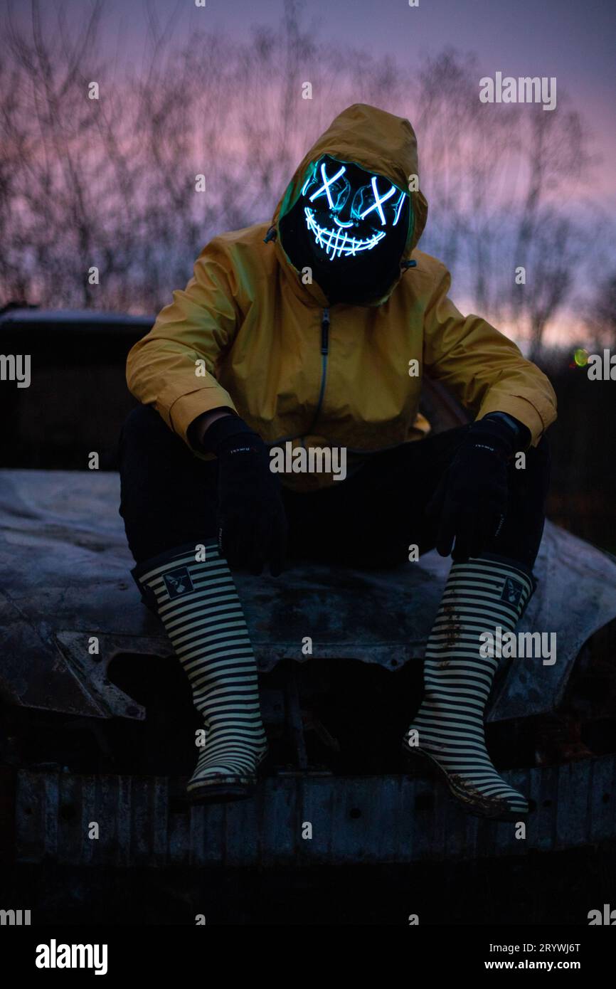 Destruction in the Night: Person with Purge Mask on a Burnt-Out Car ...