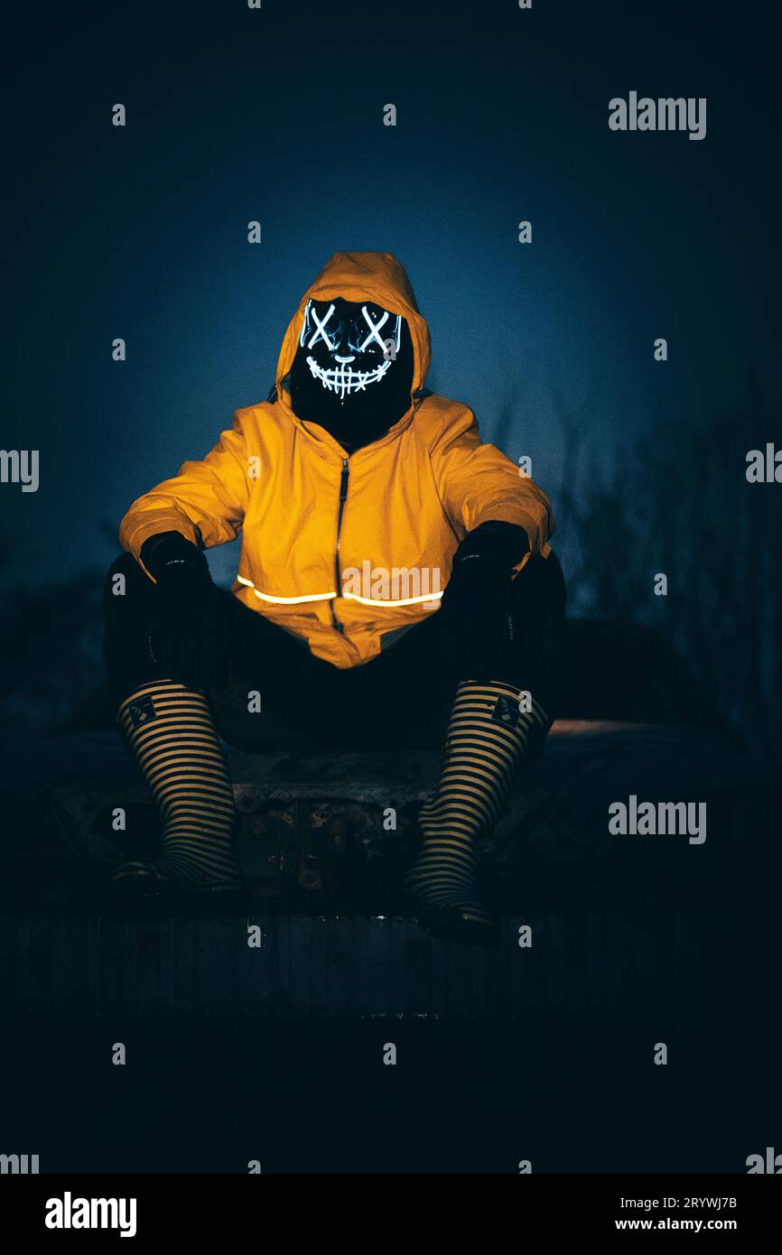 Destruction in the Night: Person with Purge Mask on a Burnt-Out Car ...