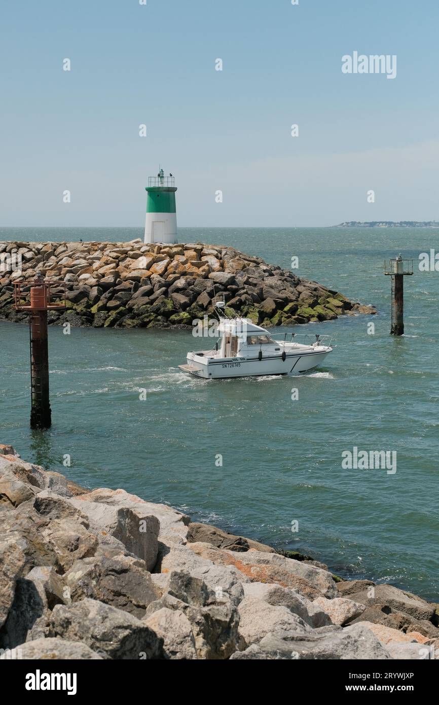 A majestic lighthouse stands amidst a rocky shoreline with a boat Stock ...