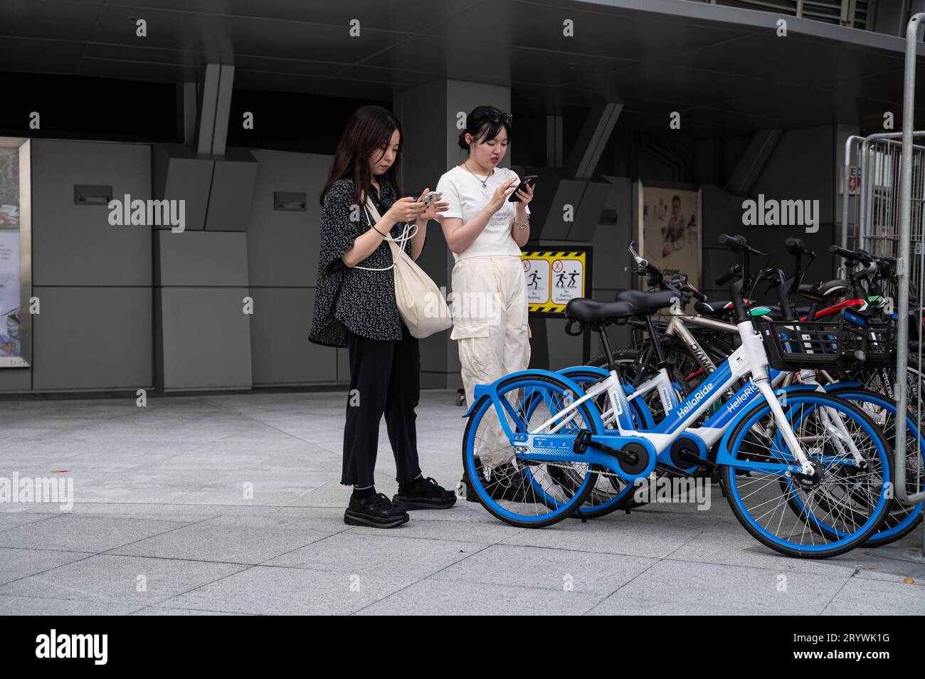 01.08.2023, Singapore, Republic of Singapore, Asia - 2 Asian tourists with mobile phones next to ...