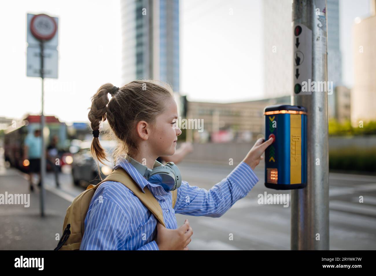 Schoolgirl standing at the crosswalk and pressing the crosswalk button ...