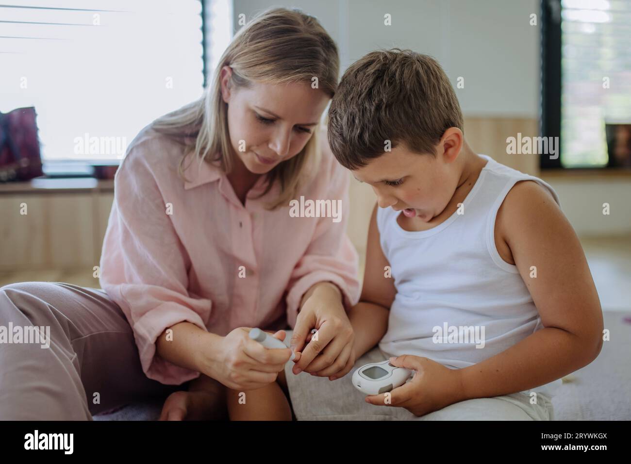 Mother checking her son's blood glucose level at home using a ...