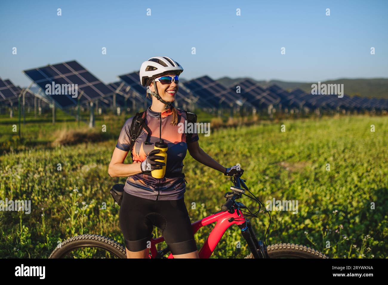 Portrait of a beautiful cyclist standing in front of solar panels at a ...