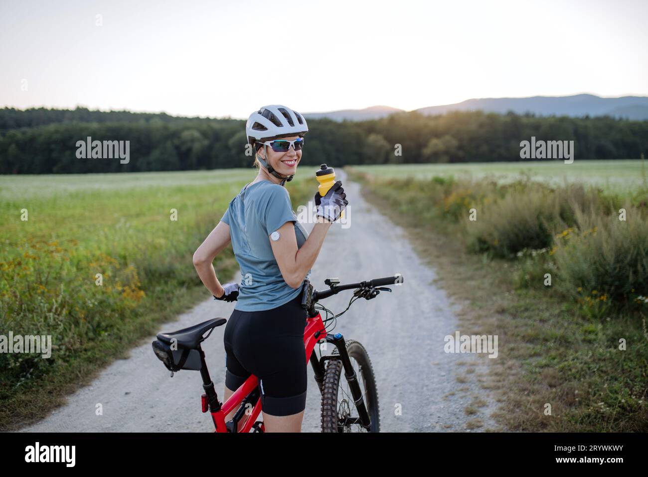 Diabetic cyclist with a continuous glucose monitor on her arm drinking ...