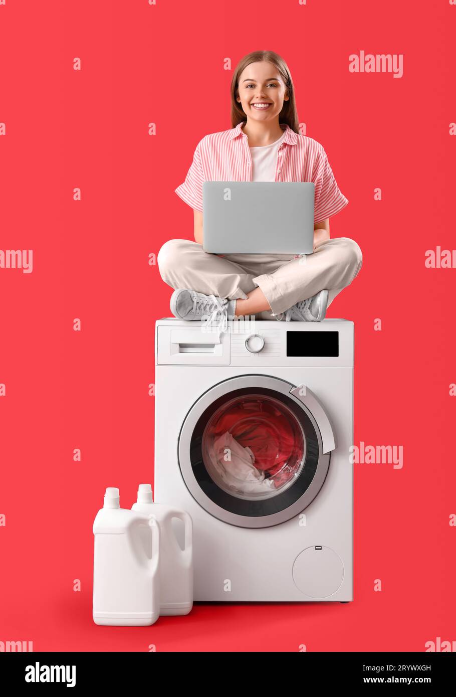 Pretty young woman with modern laptop sitting on washing machine ...