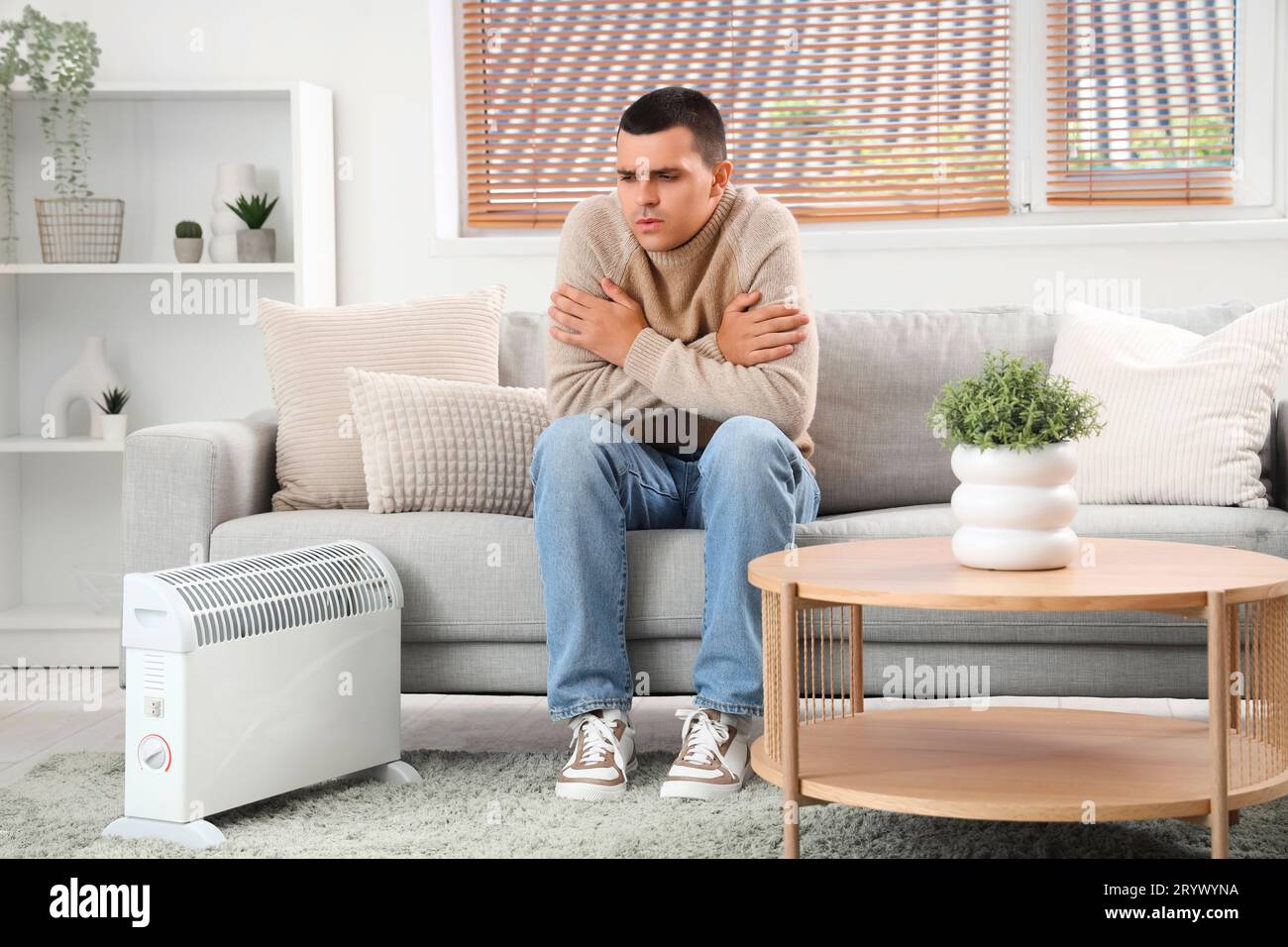 Frozen young man warming near radiator at home Stock Photo - Alamy