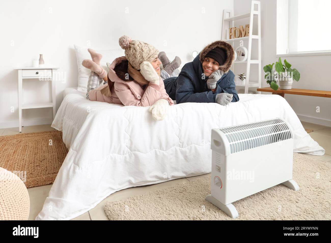 Young couple with puffers warming near radiator in bedroom Stock Photo ...