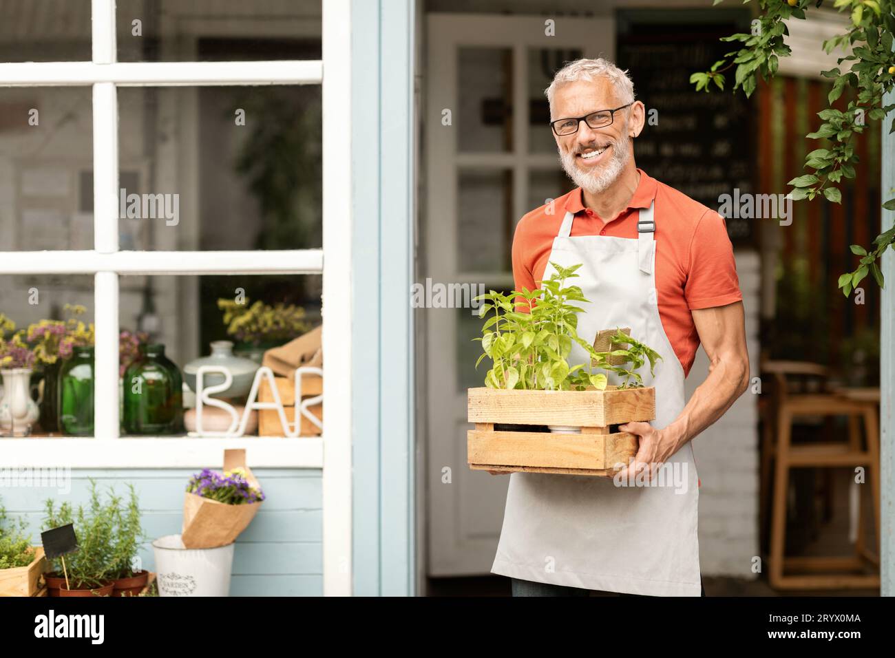 Mature Gardener Man Wearing Apron Holding Plants In Crates And Posing ...