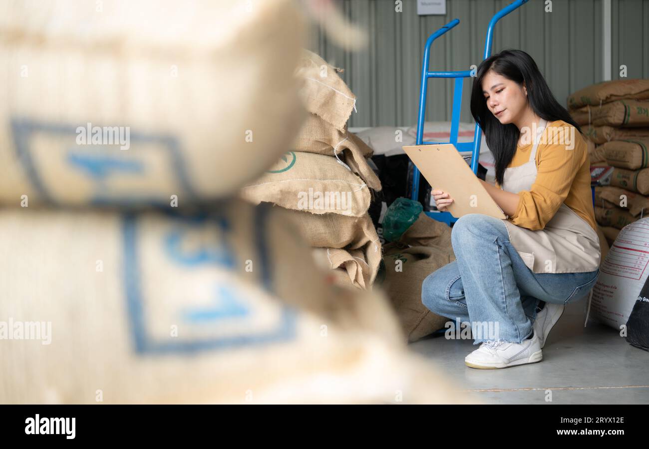 Young Asian woman sitting on the floor in coffee beans warehouse and checking documents Stock ...