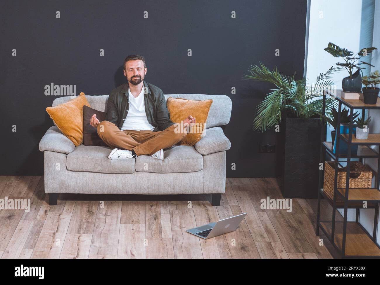 Man sitting home on couch, adopting lotus asana pose, and embracing ...