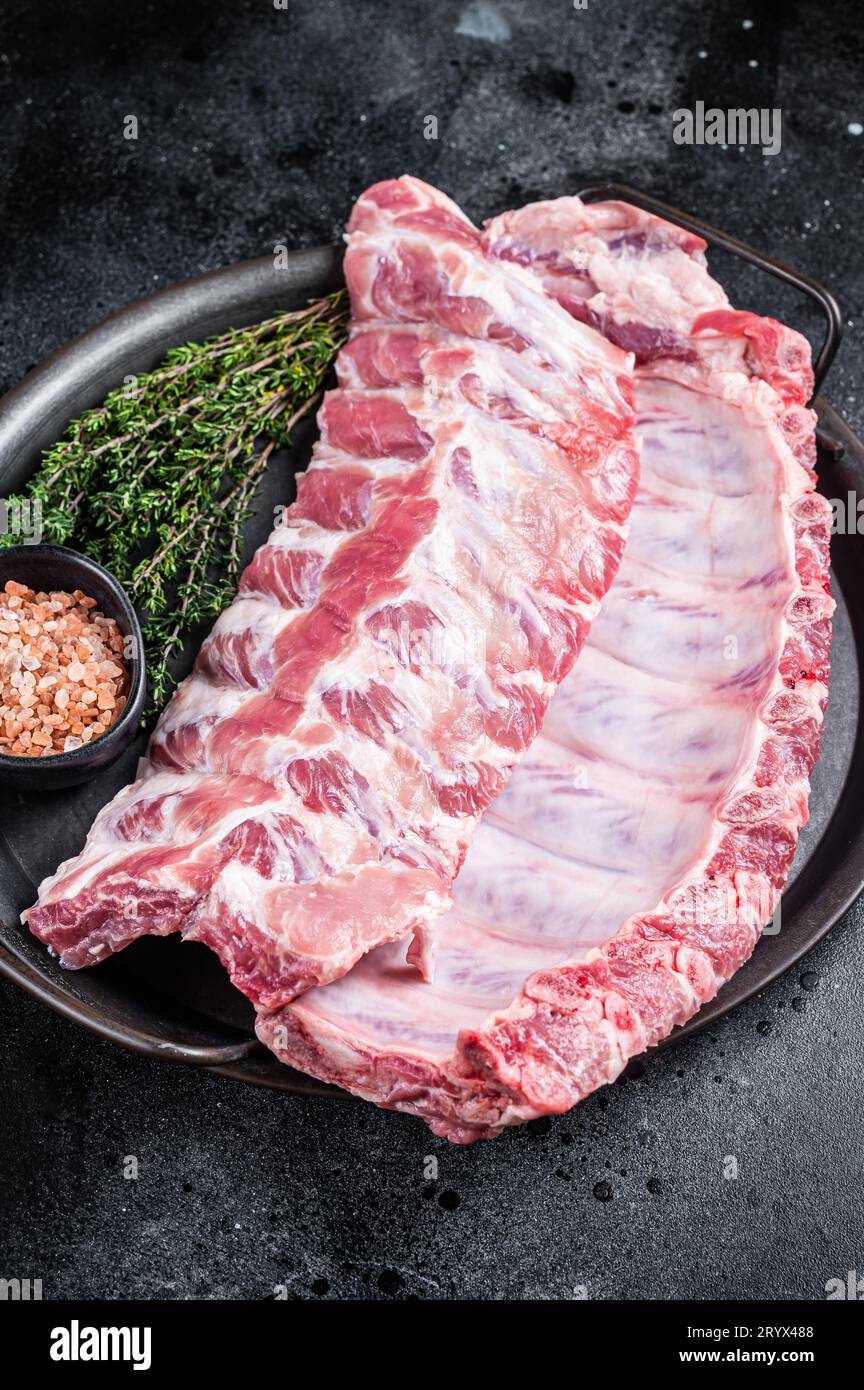 Raw rack of pork spare ribs in steel kitchen tray. Black background ...