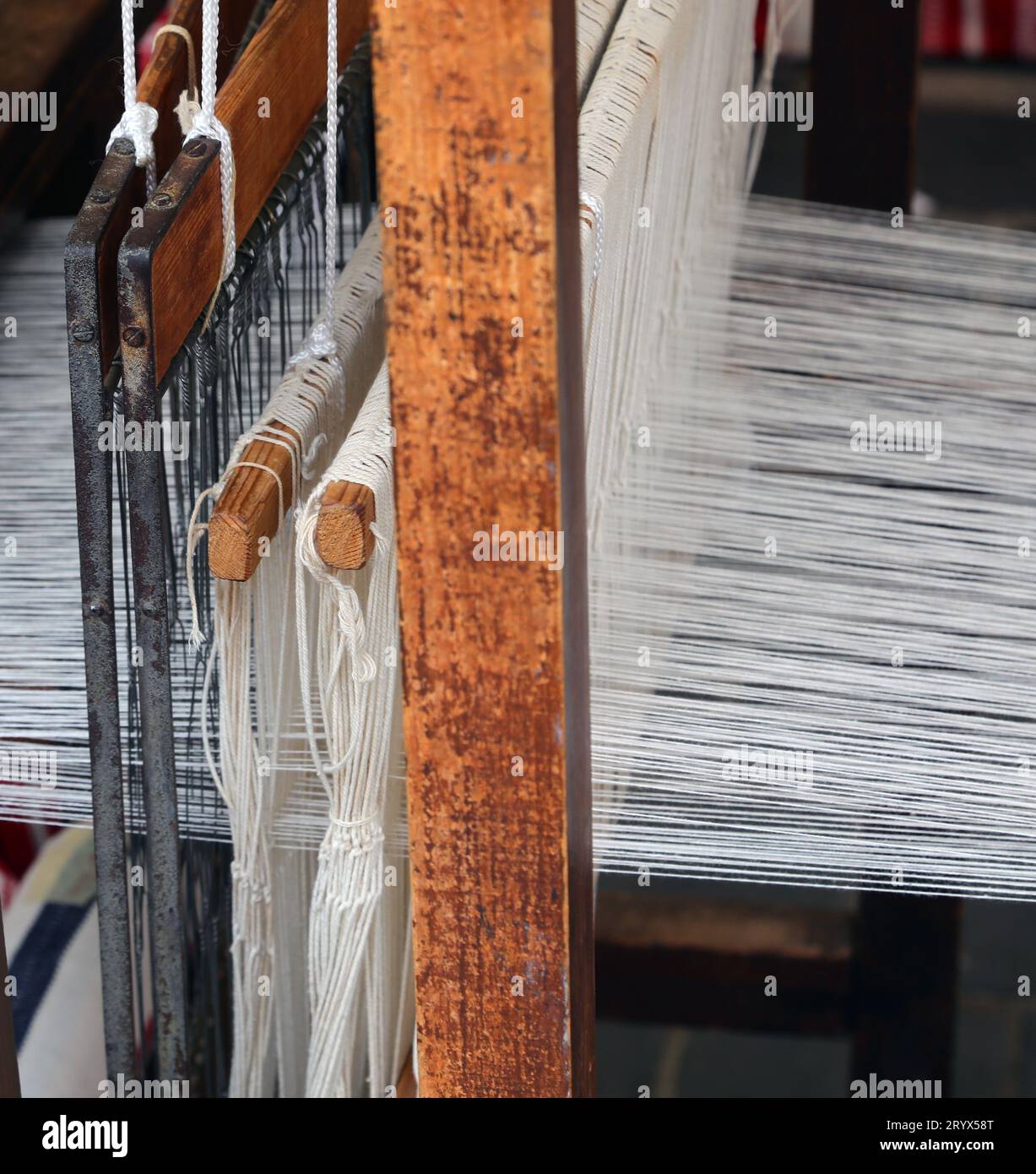 ancient wooden loom for weaving fabrics with many white threads that ...