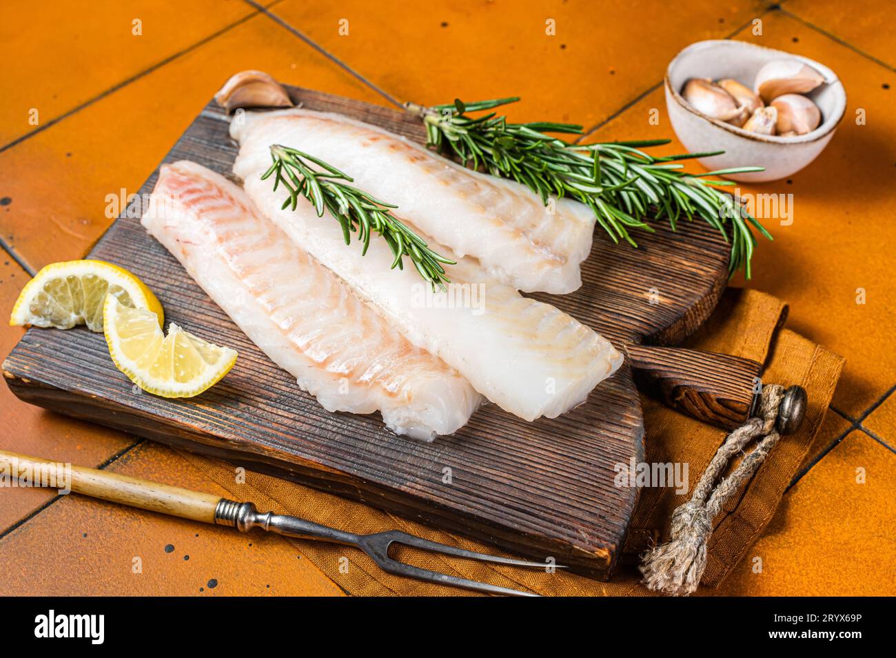 Raw cod fish fillets, codfish with rosemary on wooden board. Orange ...