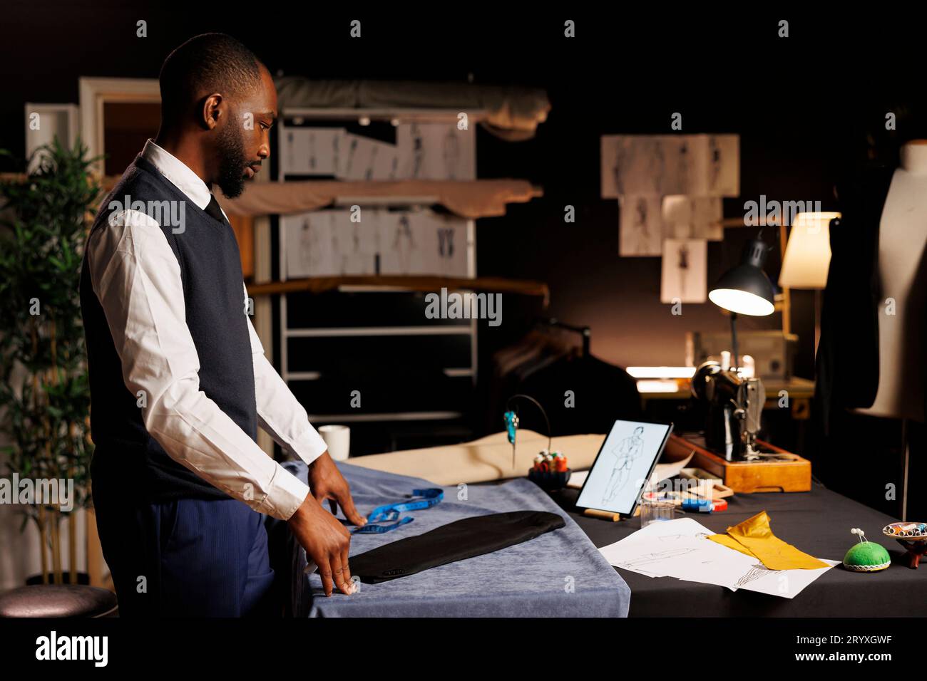 Creative couturier stiching together bespoken business suit, looking at ...