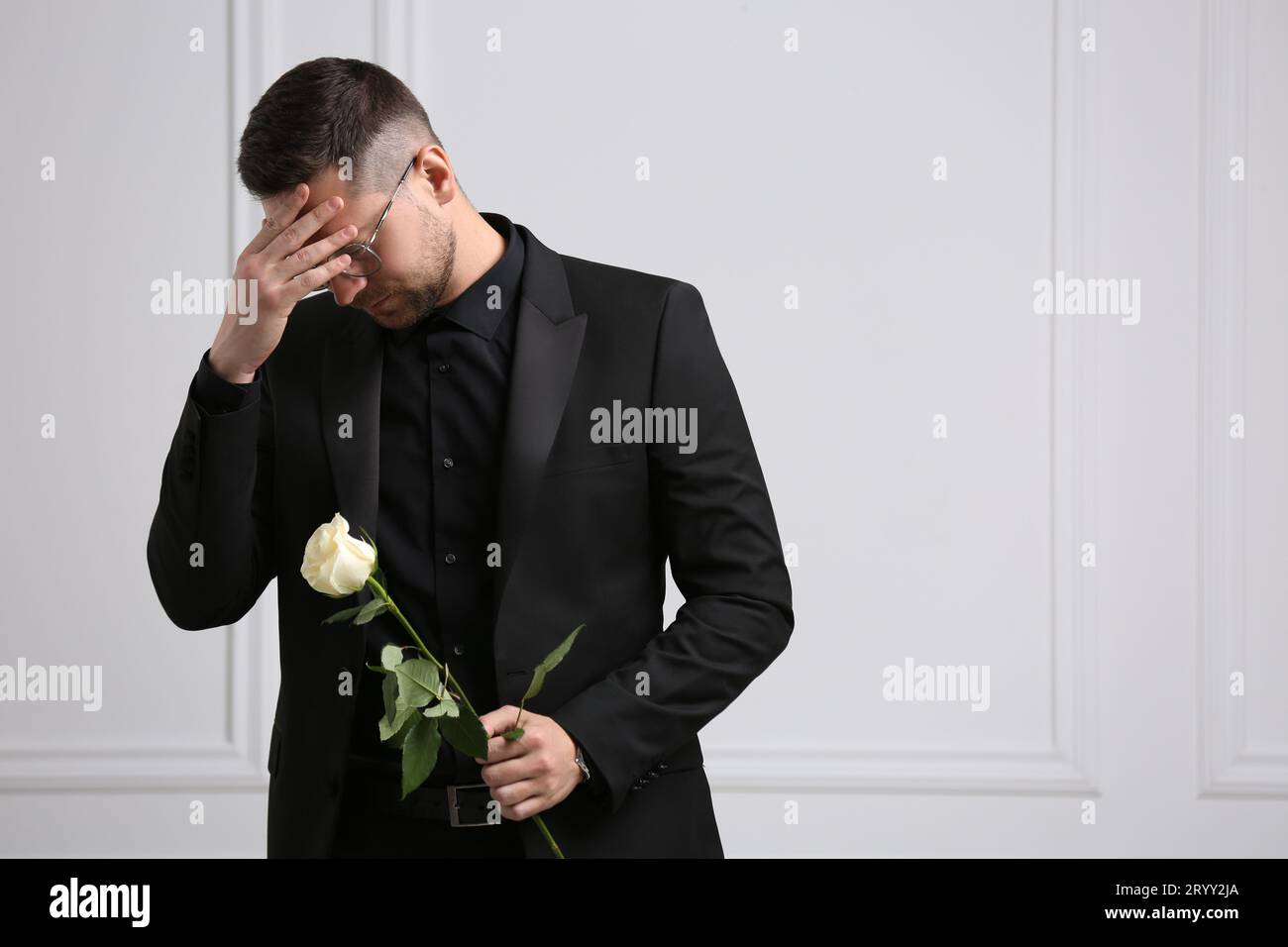 Sad man with rose flower mourning near white wall, space for text ...