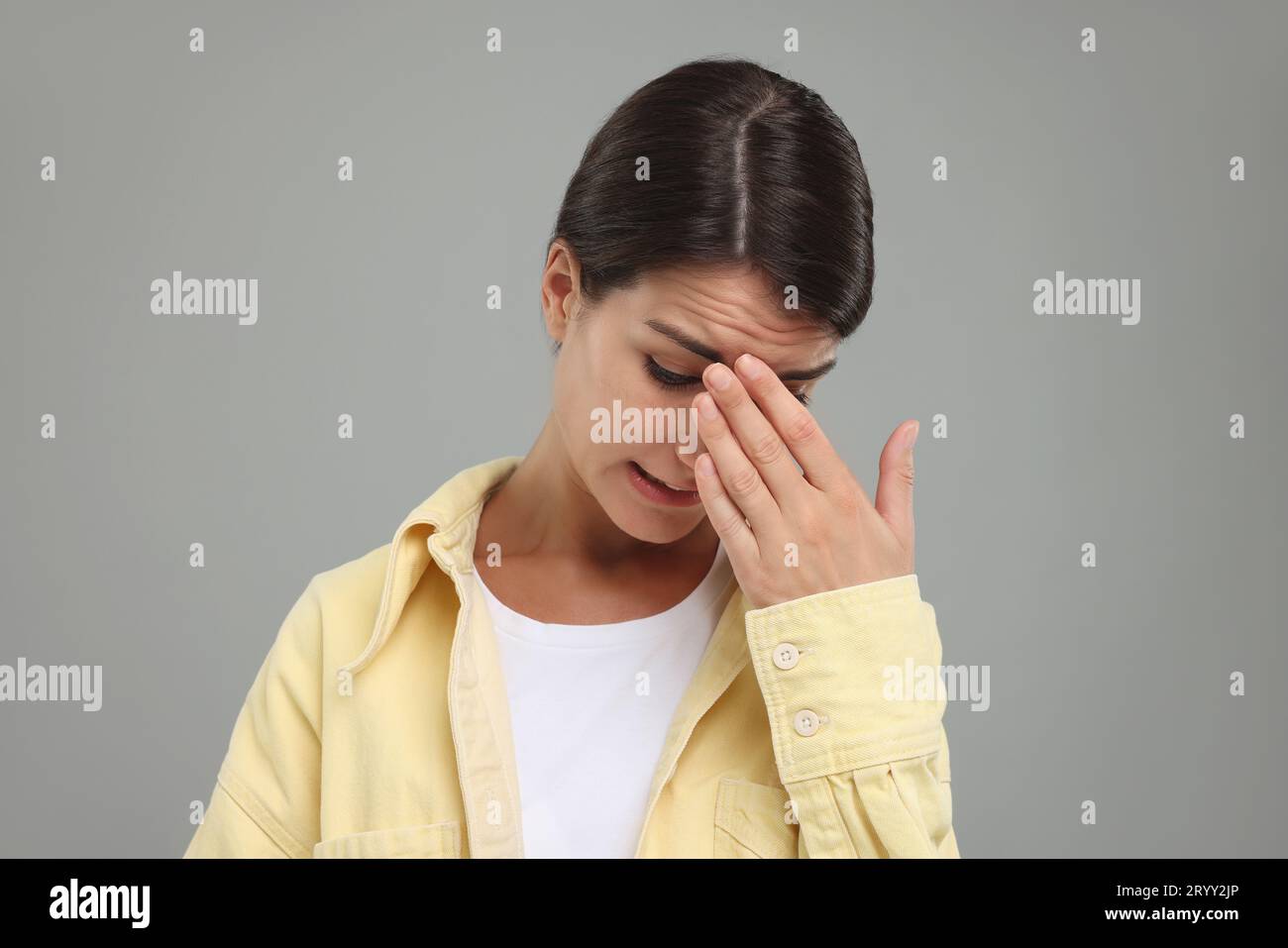 Embarrassed young woman covering face with hand on grey background ...