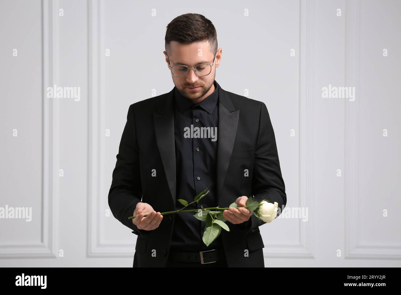 Sad man with rose flower near white wall. Funeral ceremony Stock Photo ...
