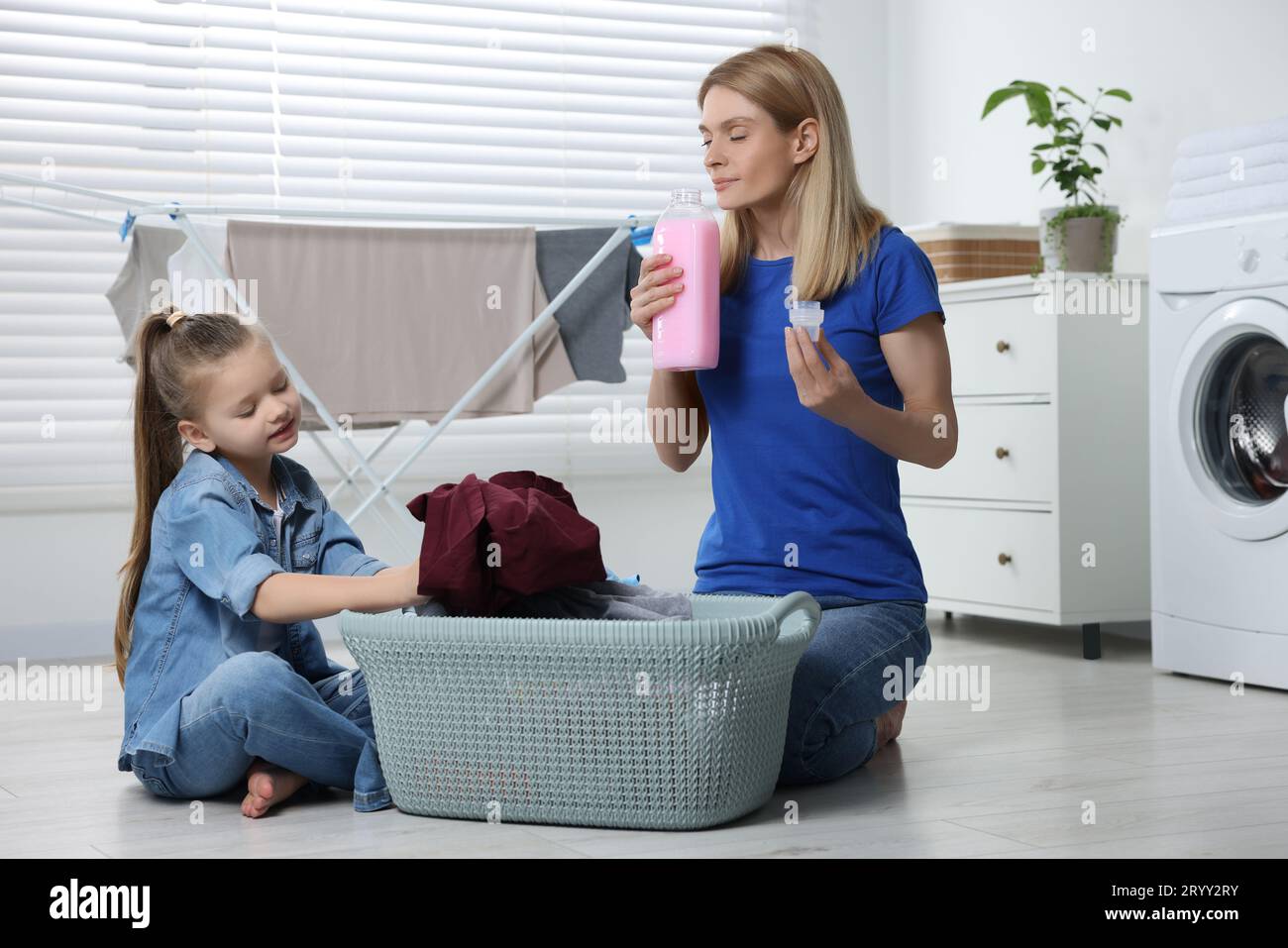 Mother smelling fabric softener while daughter taking out dirty clothes ...