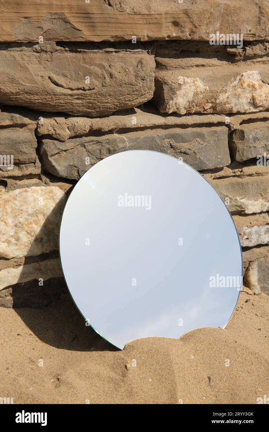 Round mirror reflecting sky on sand near stone wall outdoors Stock ...