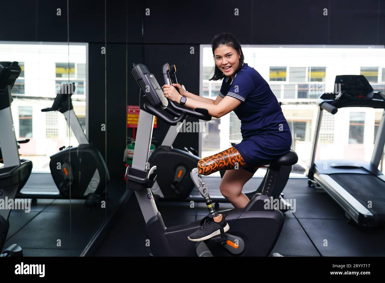 Young female with one prosthetic leg with exercising with a spinning ...