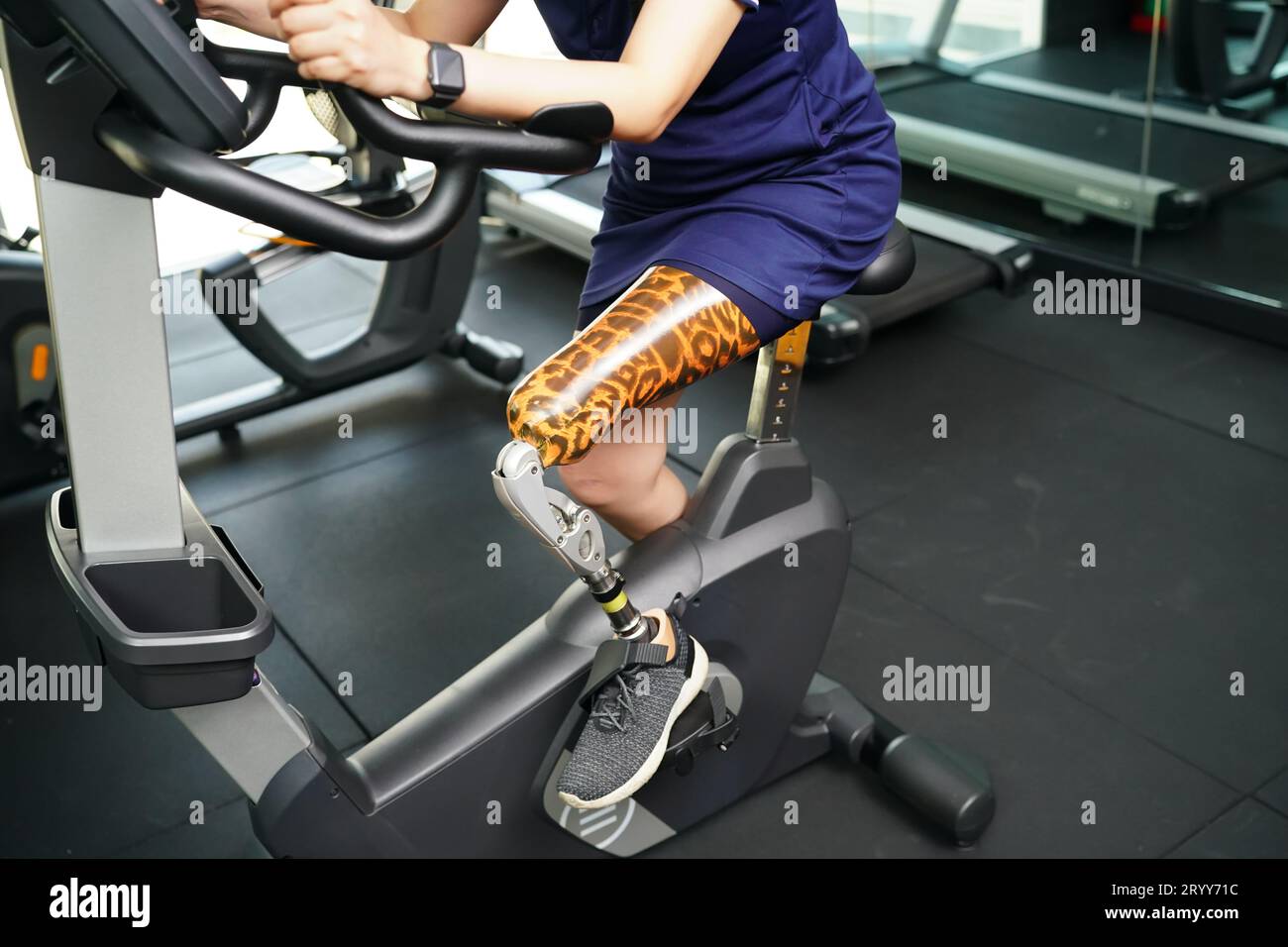 Young female with one prosthetic leg with exercising with a spinning bike in the gym to practice ...