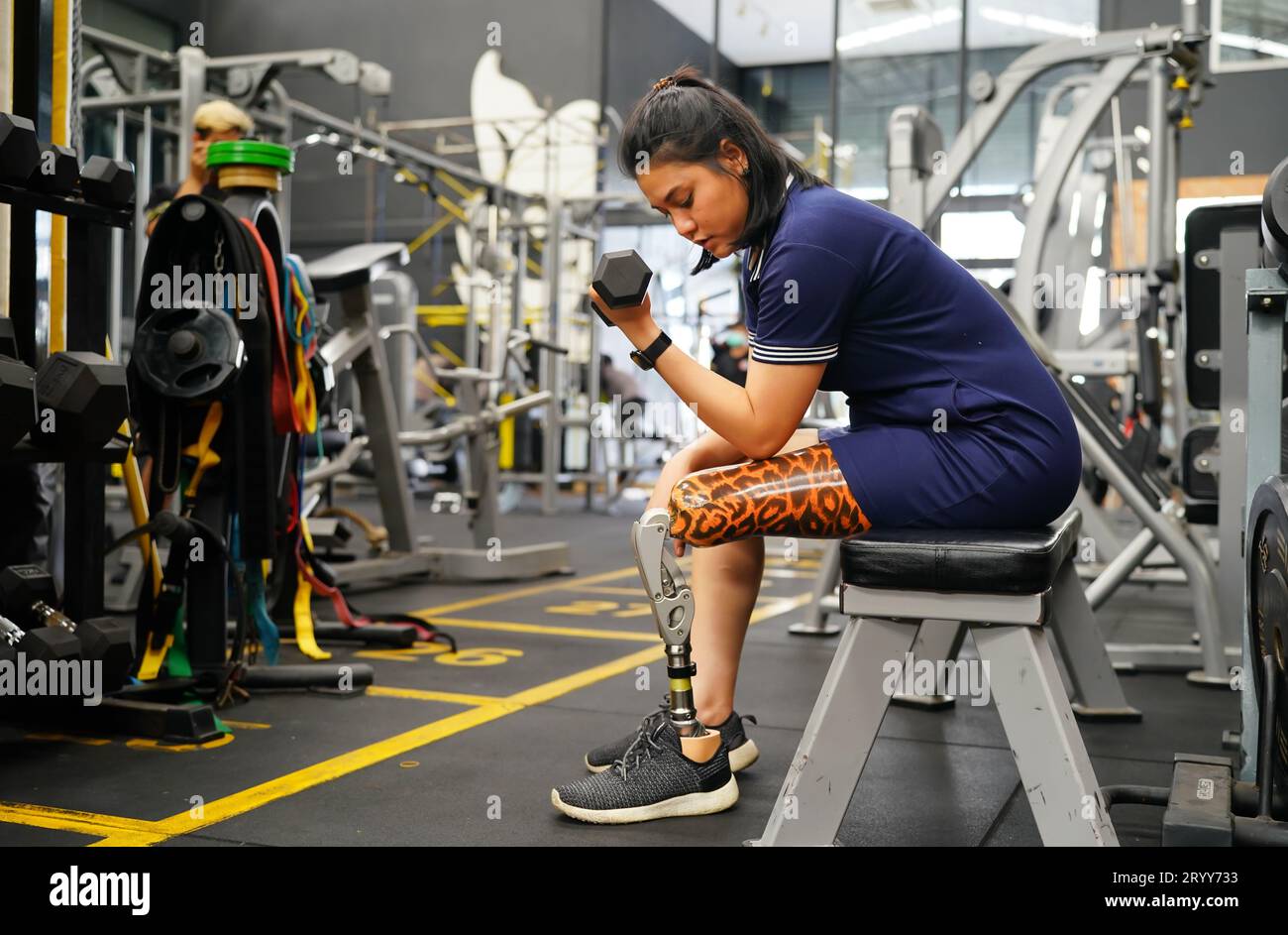 Young female with one prosthetic leg warms up by lifting light weights ...
