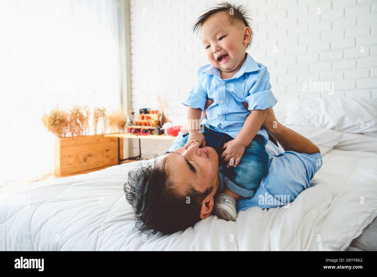 Two Asian father and his son are lying and playing in bed at bedroom ...