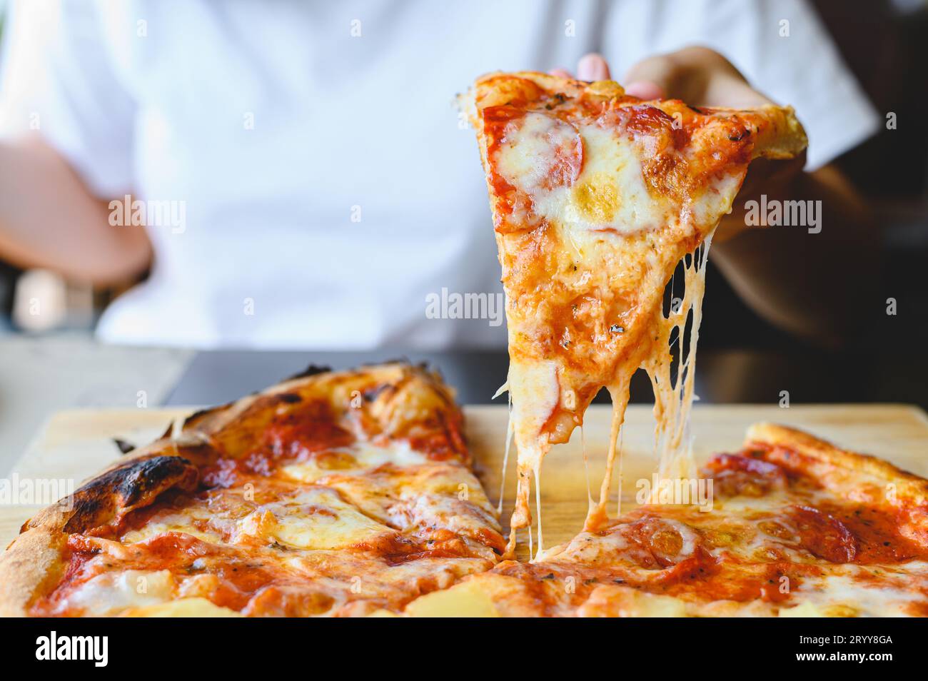 Wood fire cheesy pizza slice in hand. Traditional Hawaiian and Salami pizza savory dish flavour ...