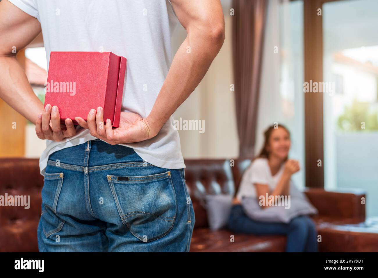 Man holding gift behind him for surprise girlfriend at their home ...