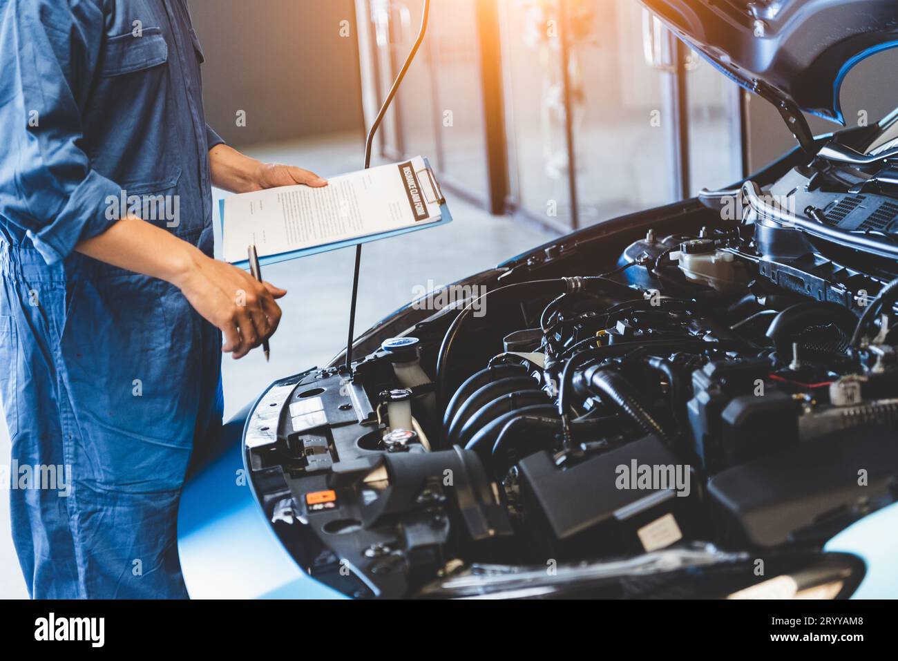 Car mechanic holding clipboard and checking to maintenance vehicle by customer claim order in ...