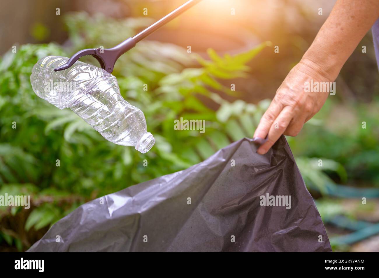 Closeup of hand and waste grabber picking up drinking plastic bottle ...