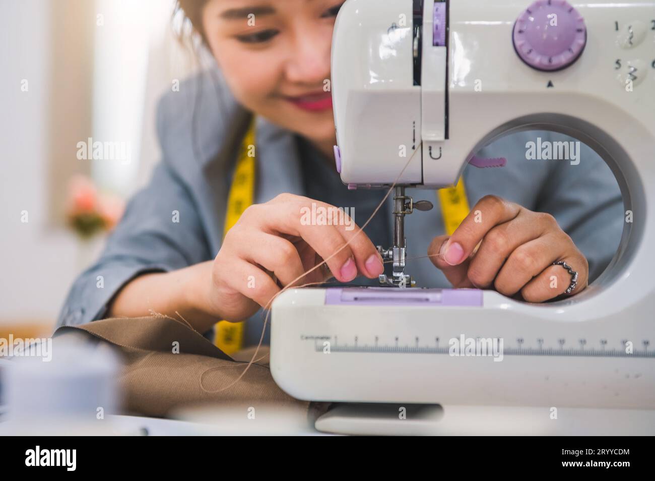 Closeup of attractive female fashion designer hand working workshop with sewing machine. Stylish ...