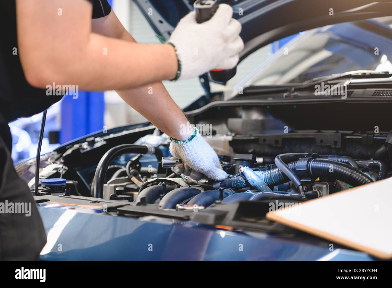 Asian male mechanic hold and shining flashlight to examine car engine ...