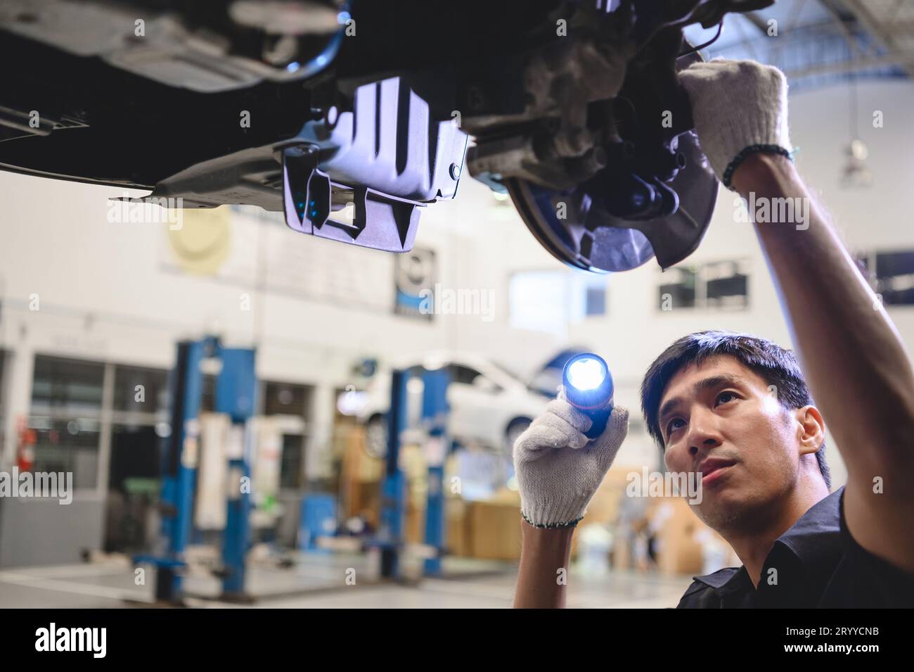 Asian male mechanical hold and shining flashlight to examine car disk ...