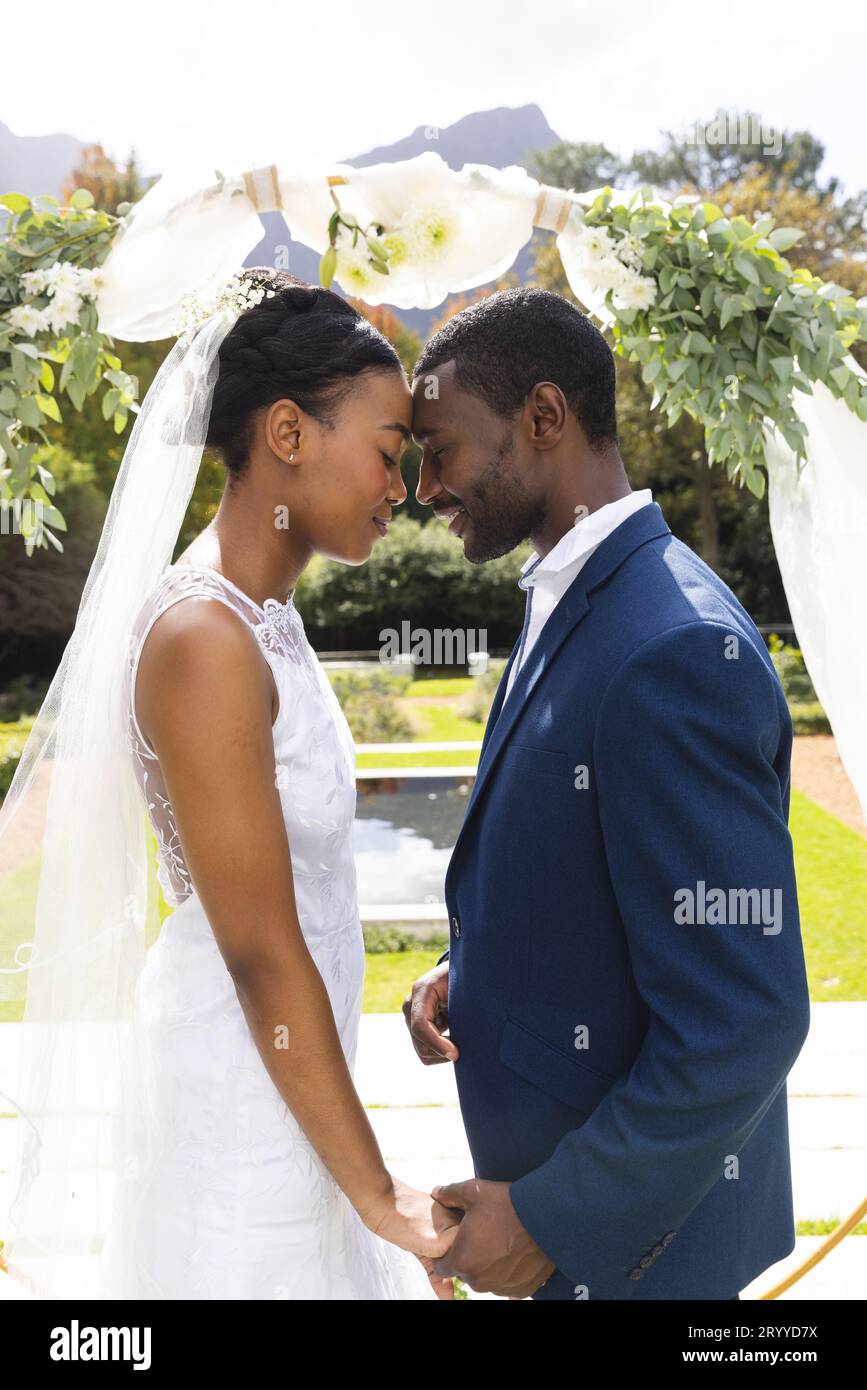 Happy african american bride and groom touching heads, holding hands by ...