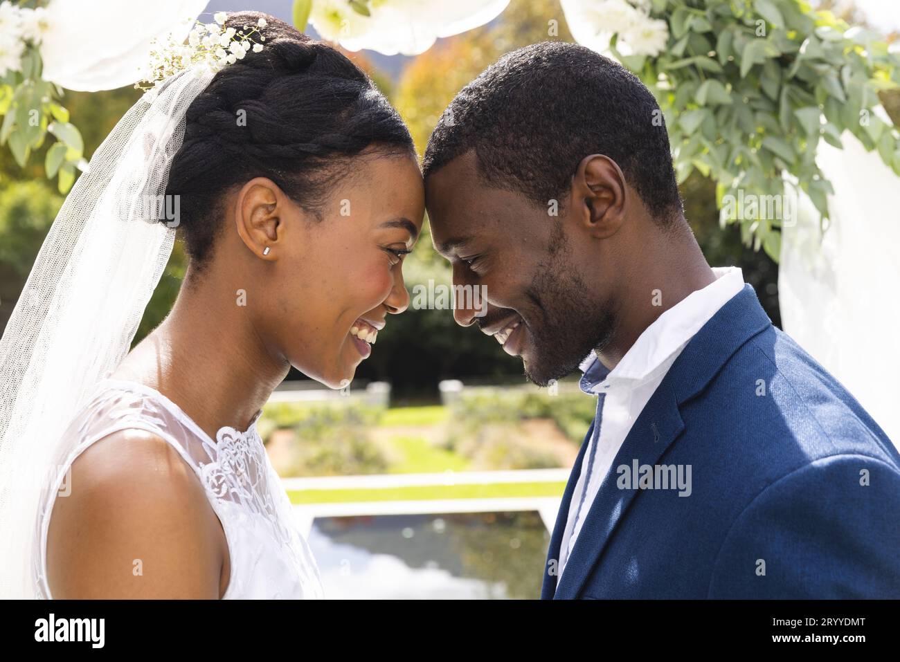 Happy african american bride and groom touching heads and smiling under ...