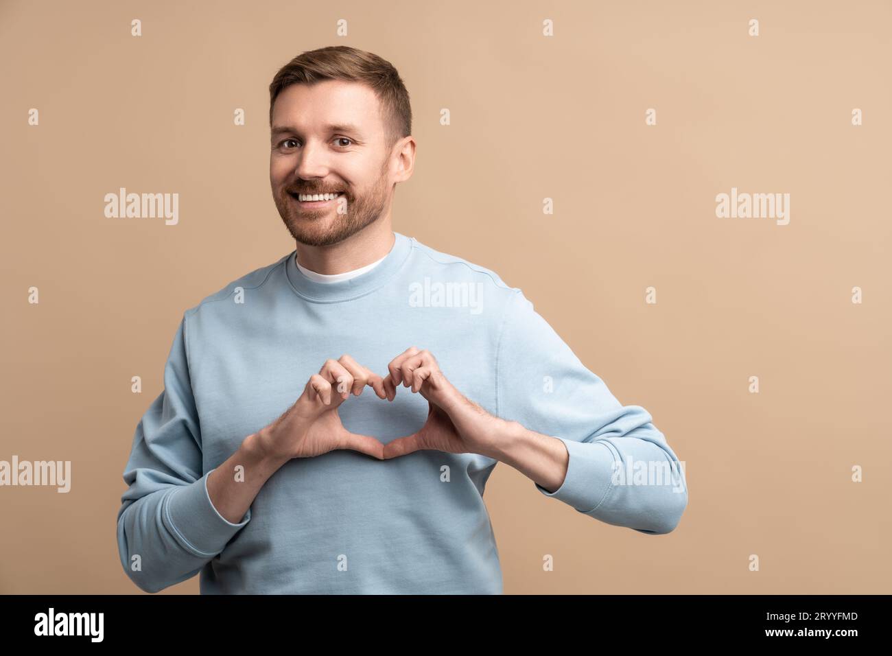 Smiling man showing heart sign hand gesture on chest on beige ...