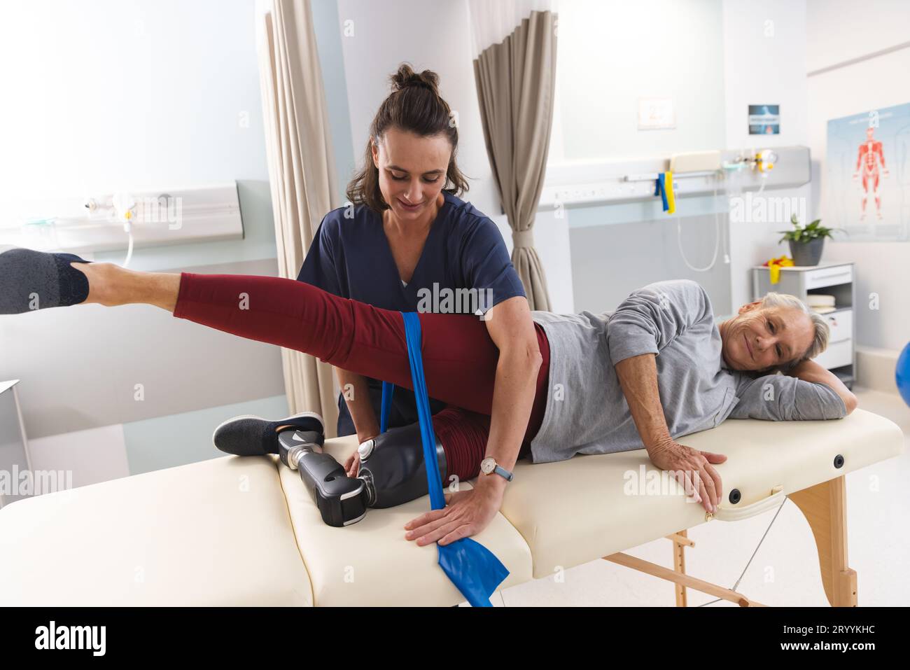 Caucasian female physiotherapist and senior woman with artificial leg using exercise band ...