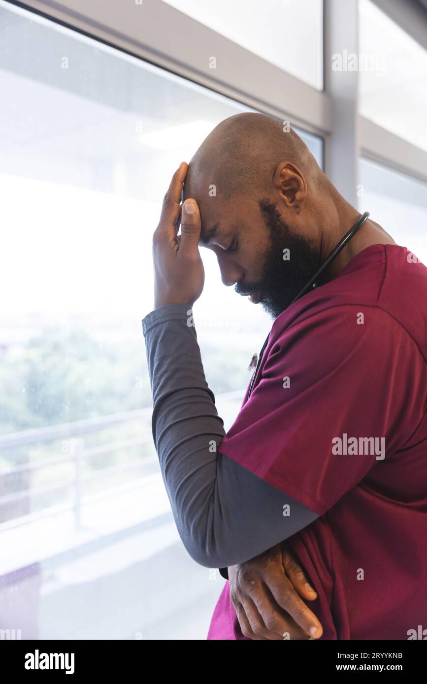 Sad african american male doctor wearing scrubs looking through window ...