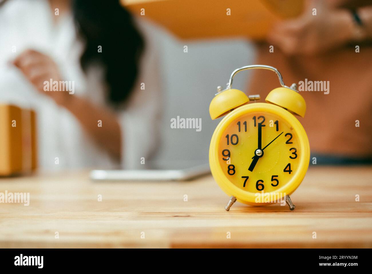 Yellow alarm clock on wooden table in office. Women checking product ...