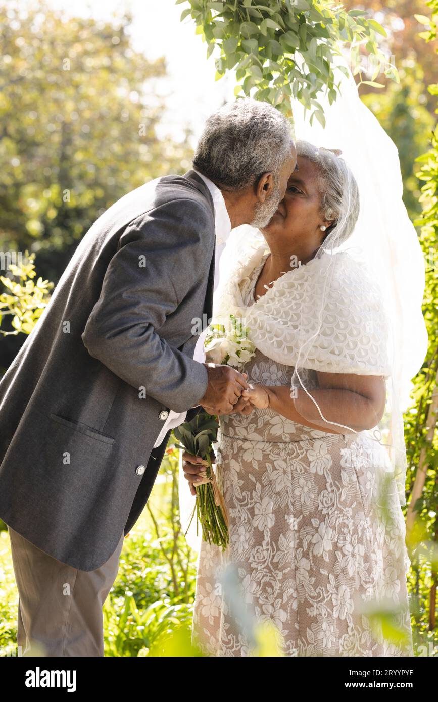 Happy senior biracial bride and groom kissing at wedding ceremony in ...