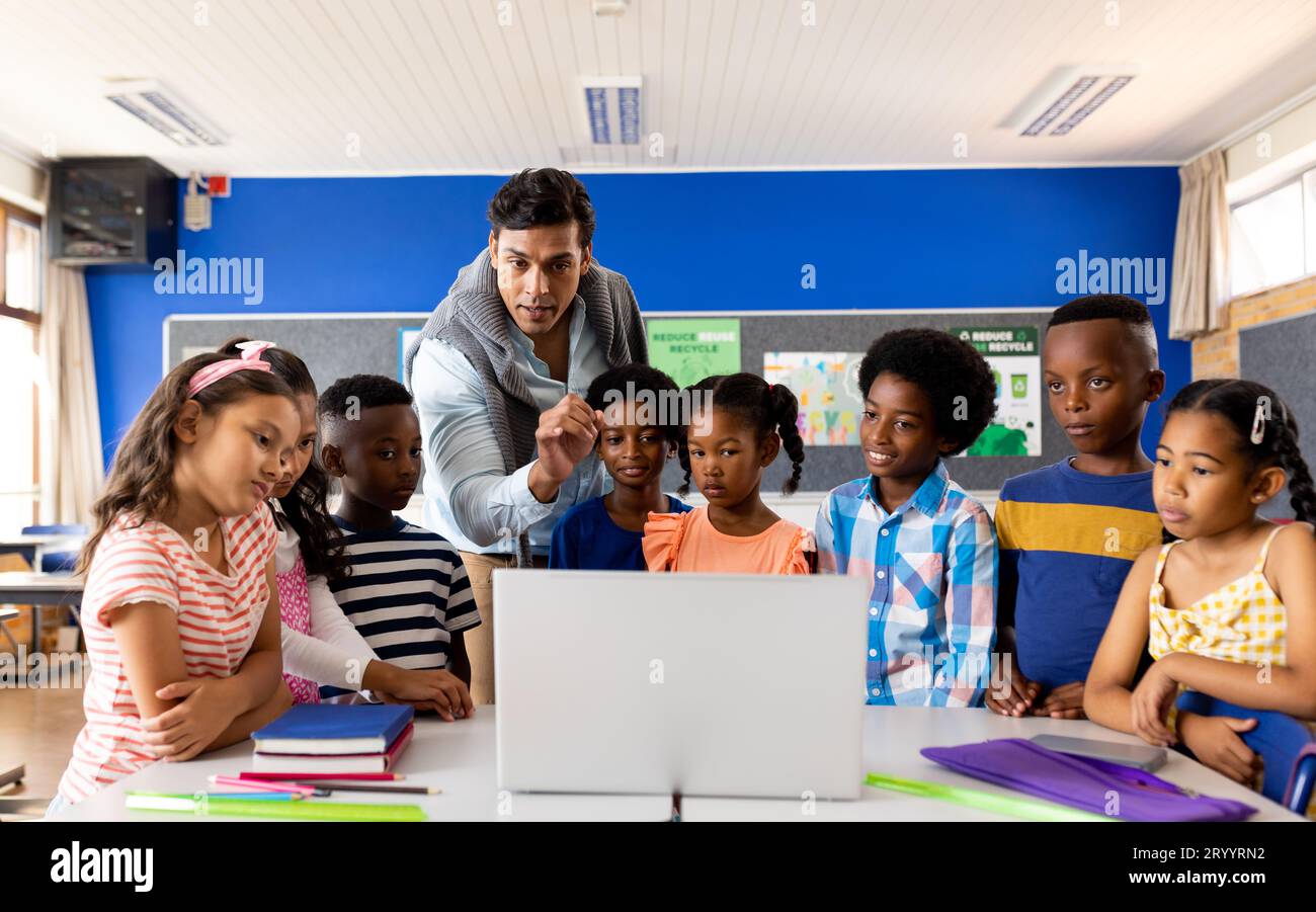 Biracial male teacher using laptop teaching children in elementary ...