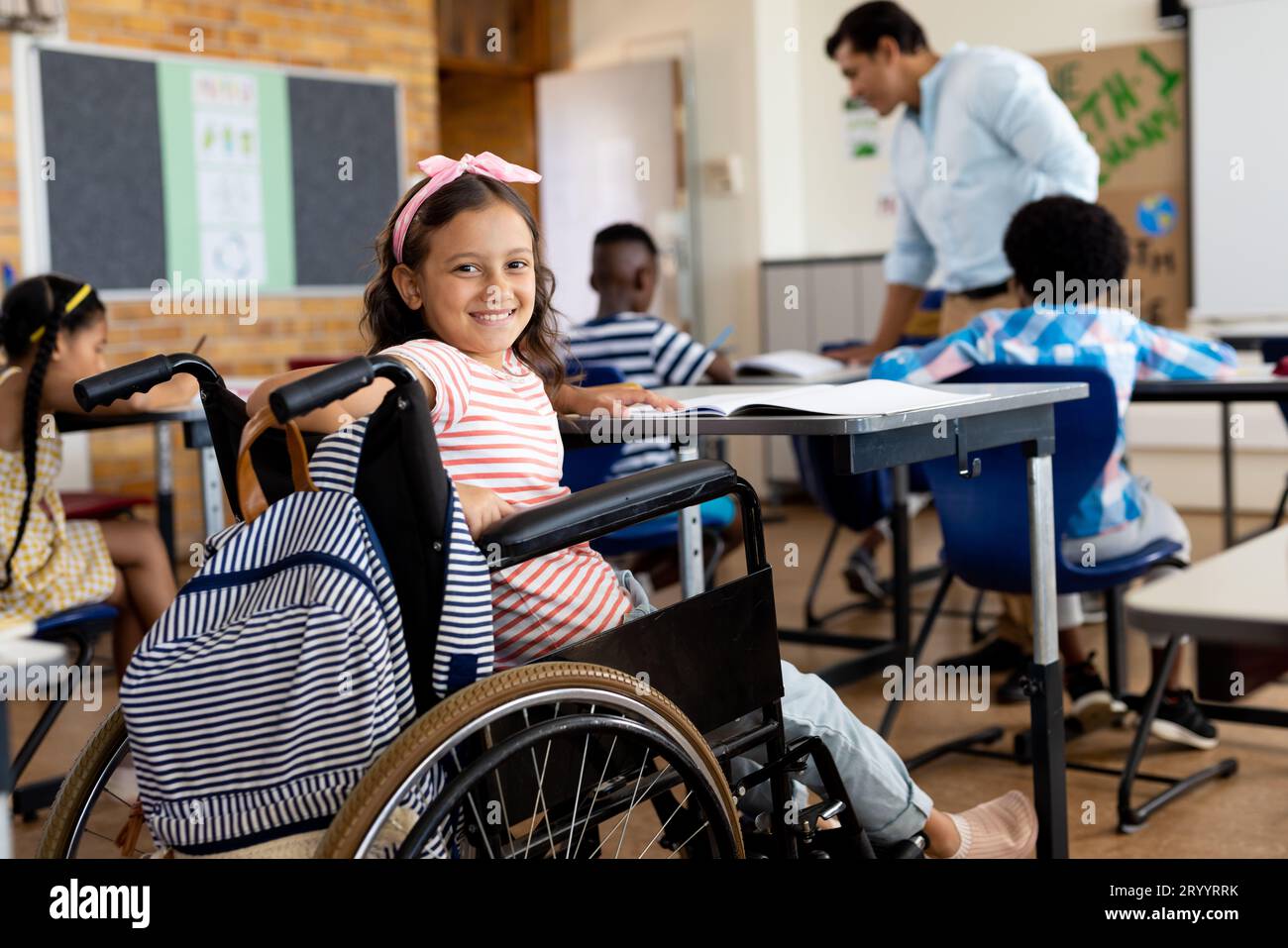 Portrait of happy biracial school girl sitting in wheelchair in class at elementary school Stock ...
