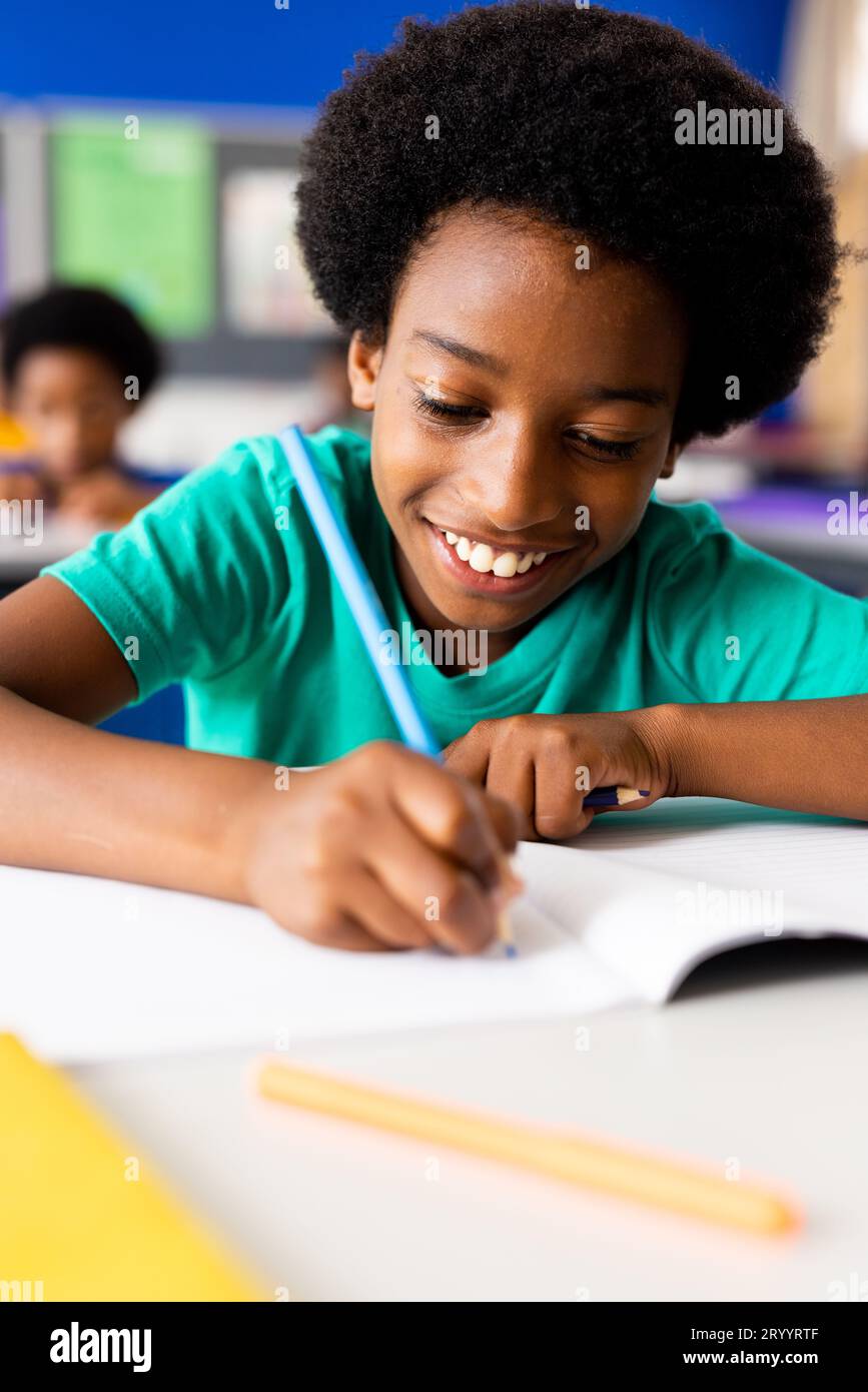 Portrait of happy african american elementary schoolboy writing in ...