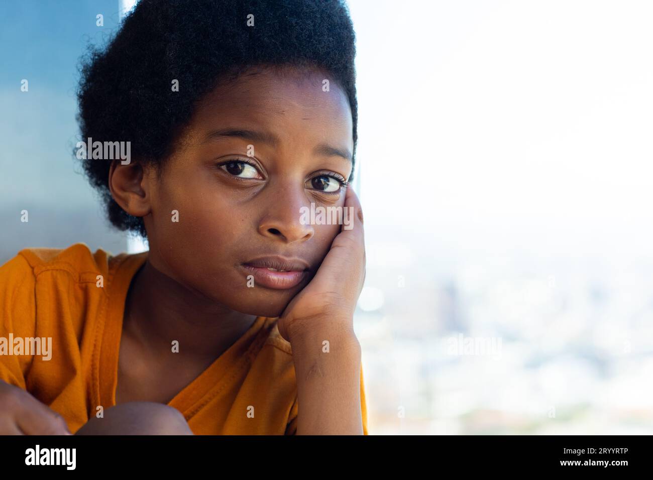 Sad biracial schoolboy wearing yellow tshirt looking through window in ...